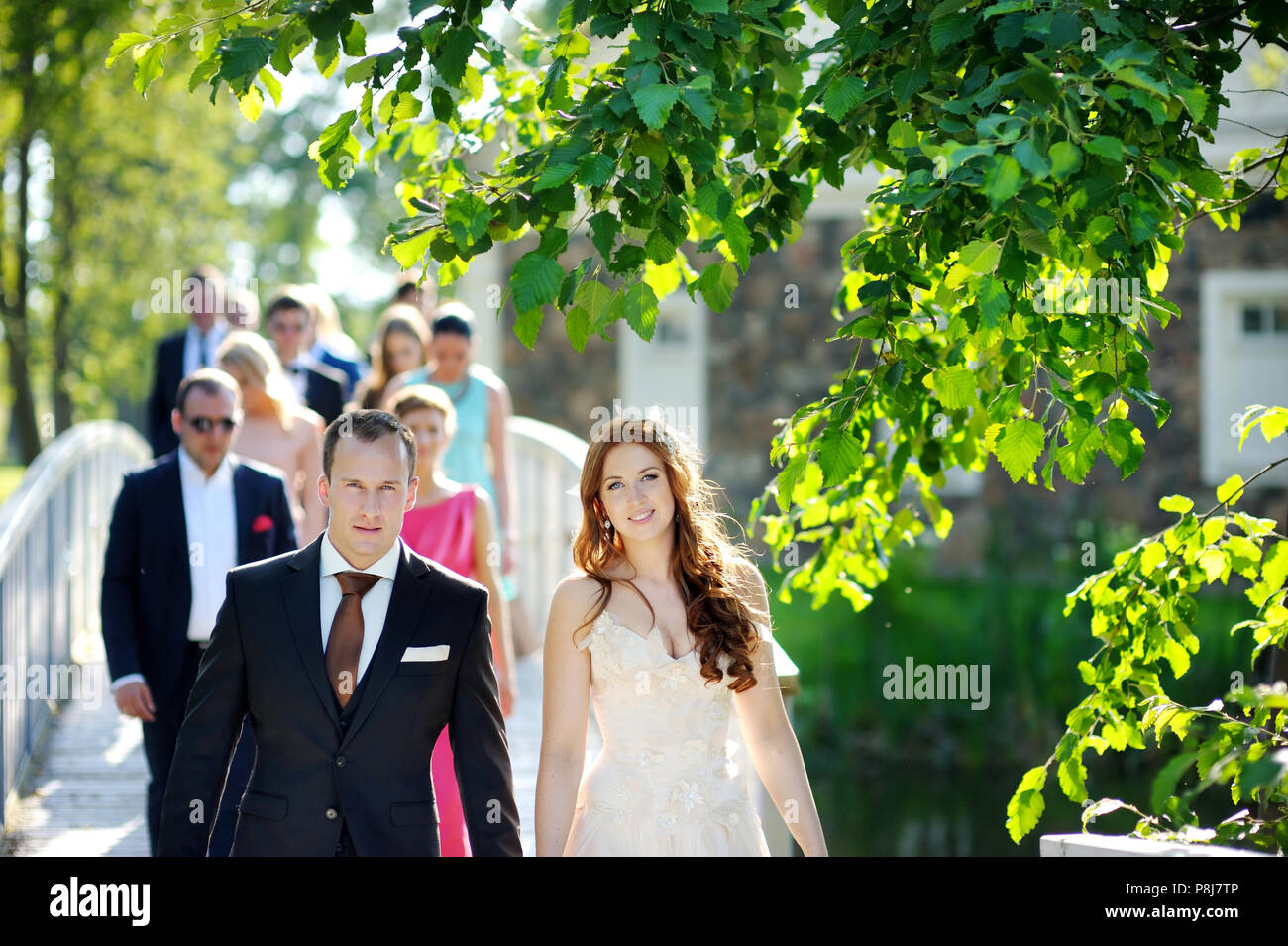 Young bride and groom and their wedding guests in beautiful summer park ...