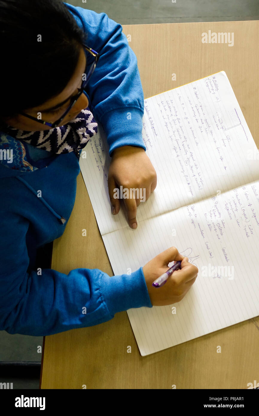A young female student taking notes in notbook using pen and copy and ...