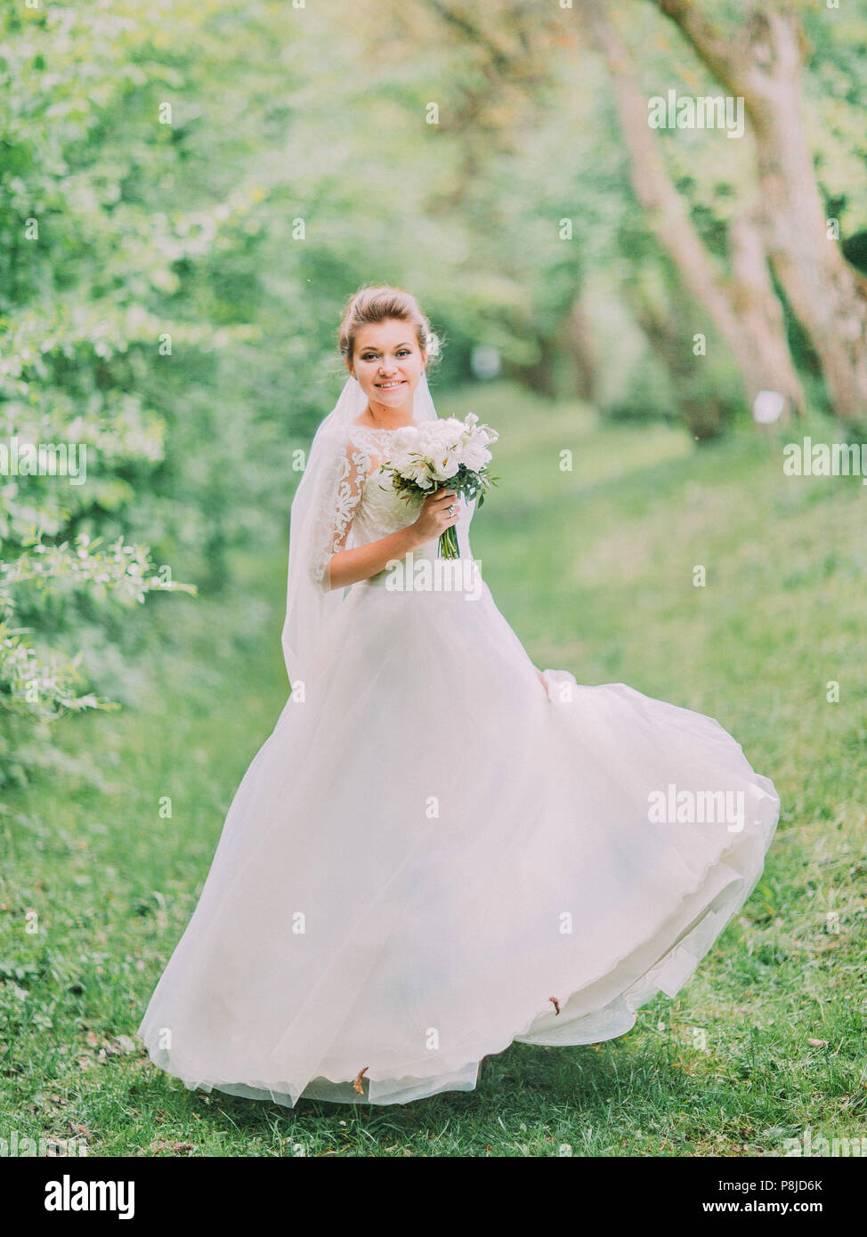 Full-length view of the smiling bride playing with the wedding dress in ...