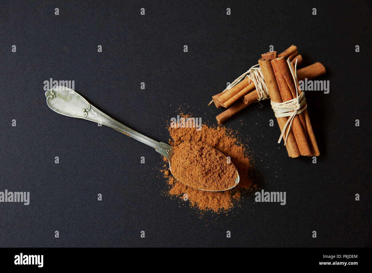 Spoonful cinnamon powder with bunch of cinnamon sticks on black ...