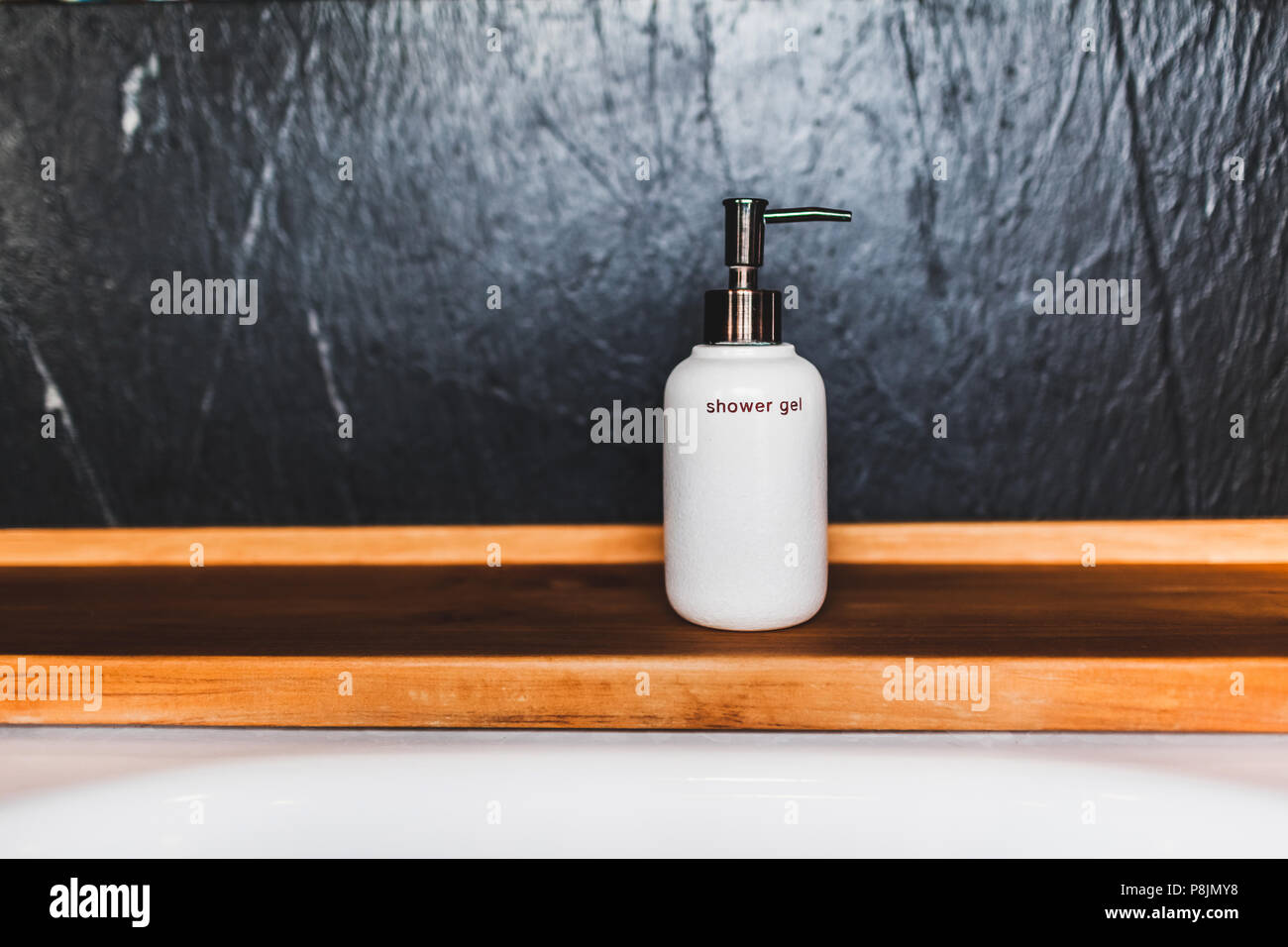 White metal bottle of shower gel on wooden edge of bath in modern hotel ...