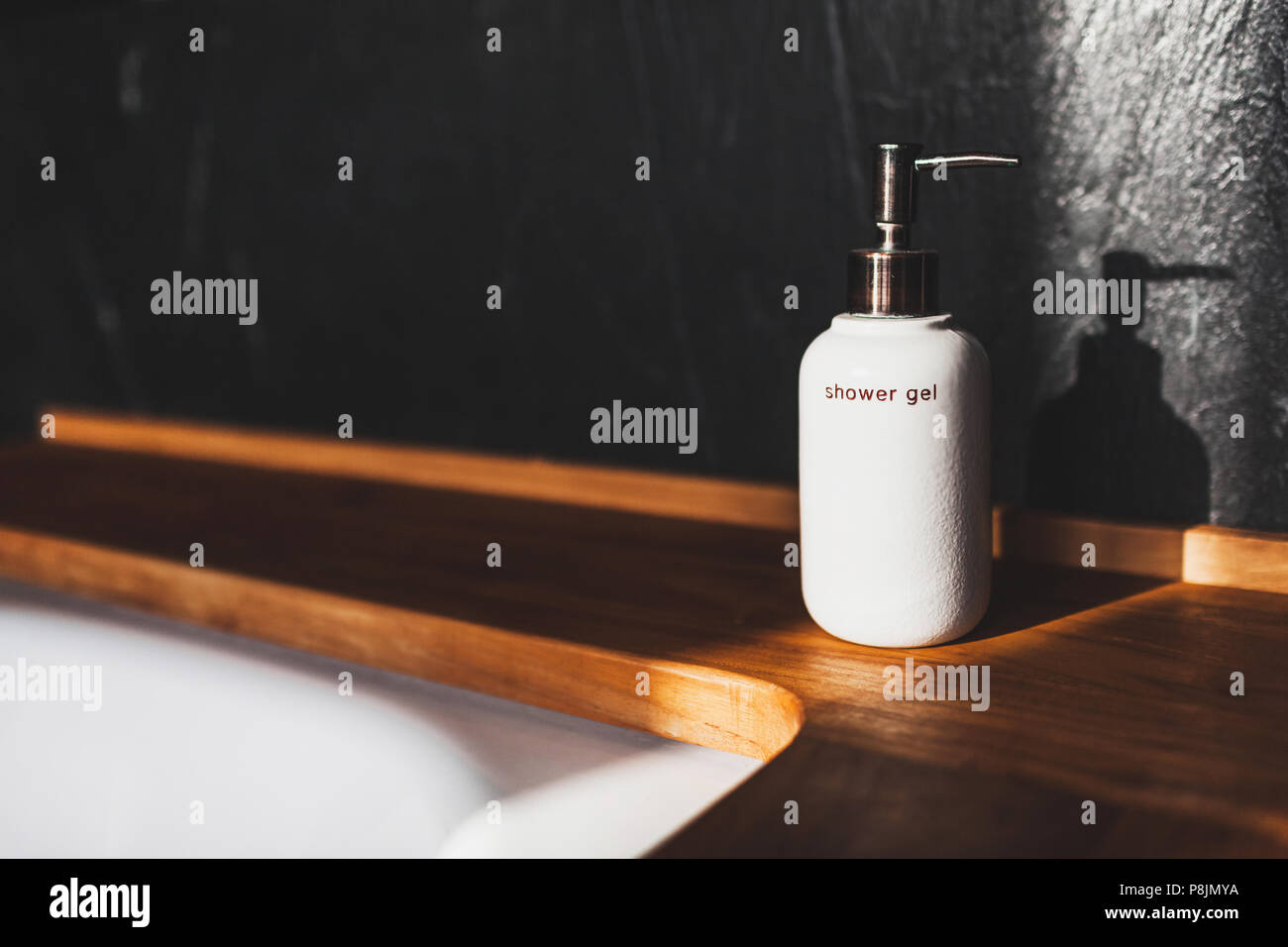 White metal bottle of shower gel on wooden edge of bath in modern hotel ...