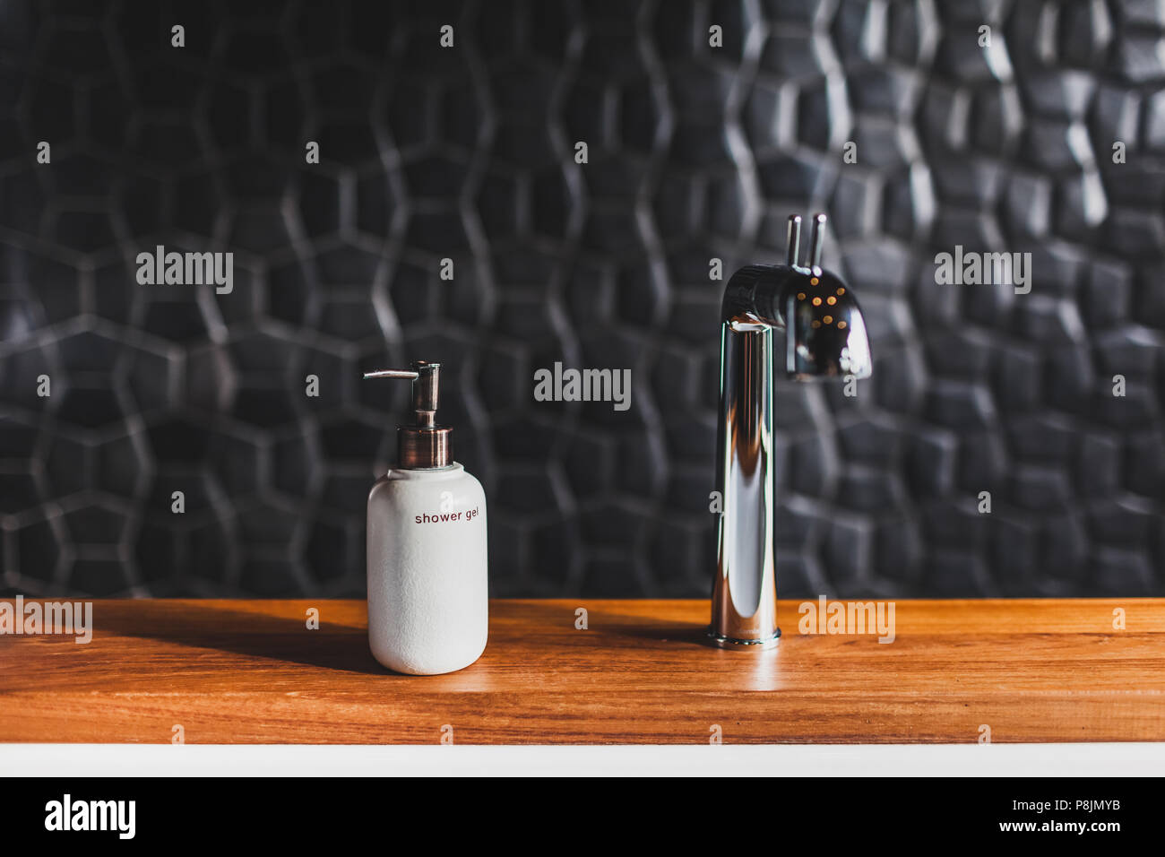 White metal bottle of shower gel on wooden edge of bath in modern hotel ...