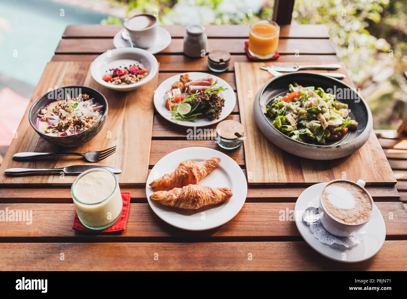 Breakfast for two on wooden table. Croissants, fresh salad, natural ...