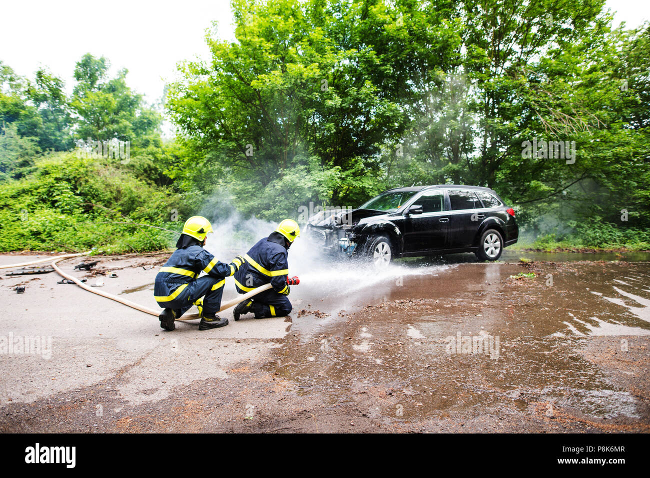Two firefighters extinguishing a burning car after an accident Stock ...