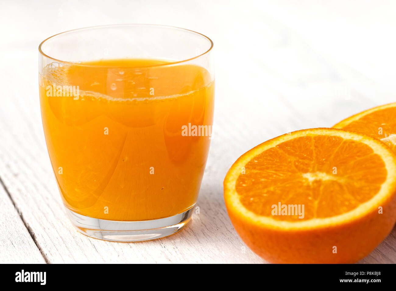 Glass of orrange juice next to halved orange. White wood background ...