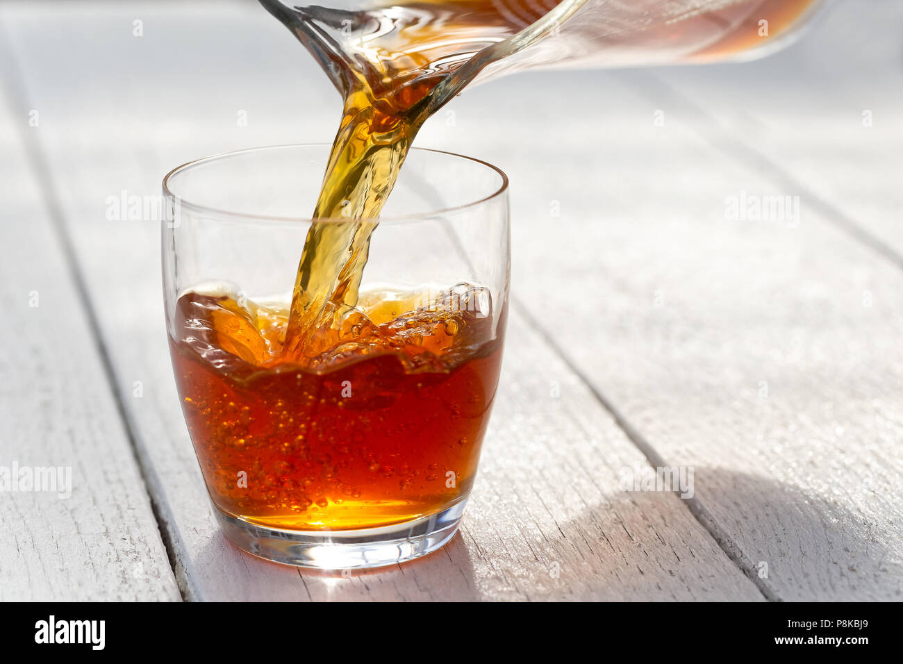 Pouring ice tea from a glass jug into a glass. White wood background ...
