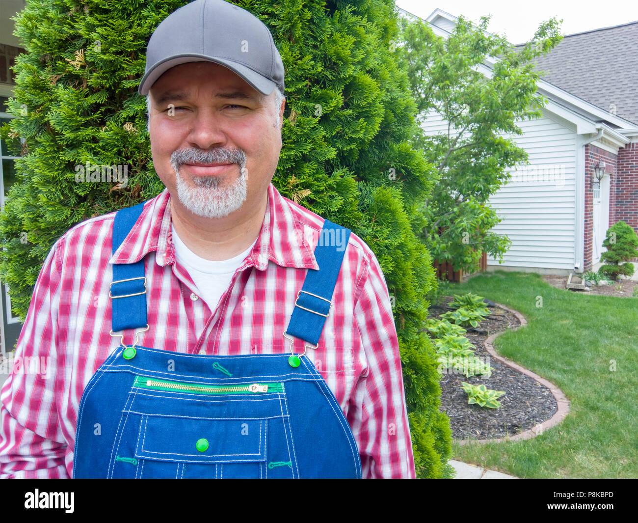 Proud happy middle-aged man in dungarees and cap standing in front of ...