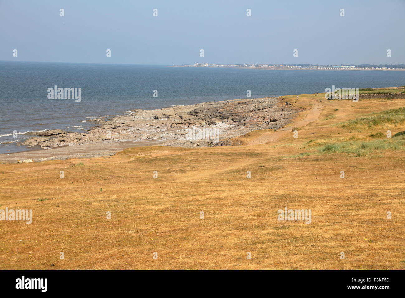 A small bay amid Ogmore by sea on a sunny day with dog walkers walking ...