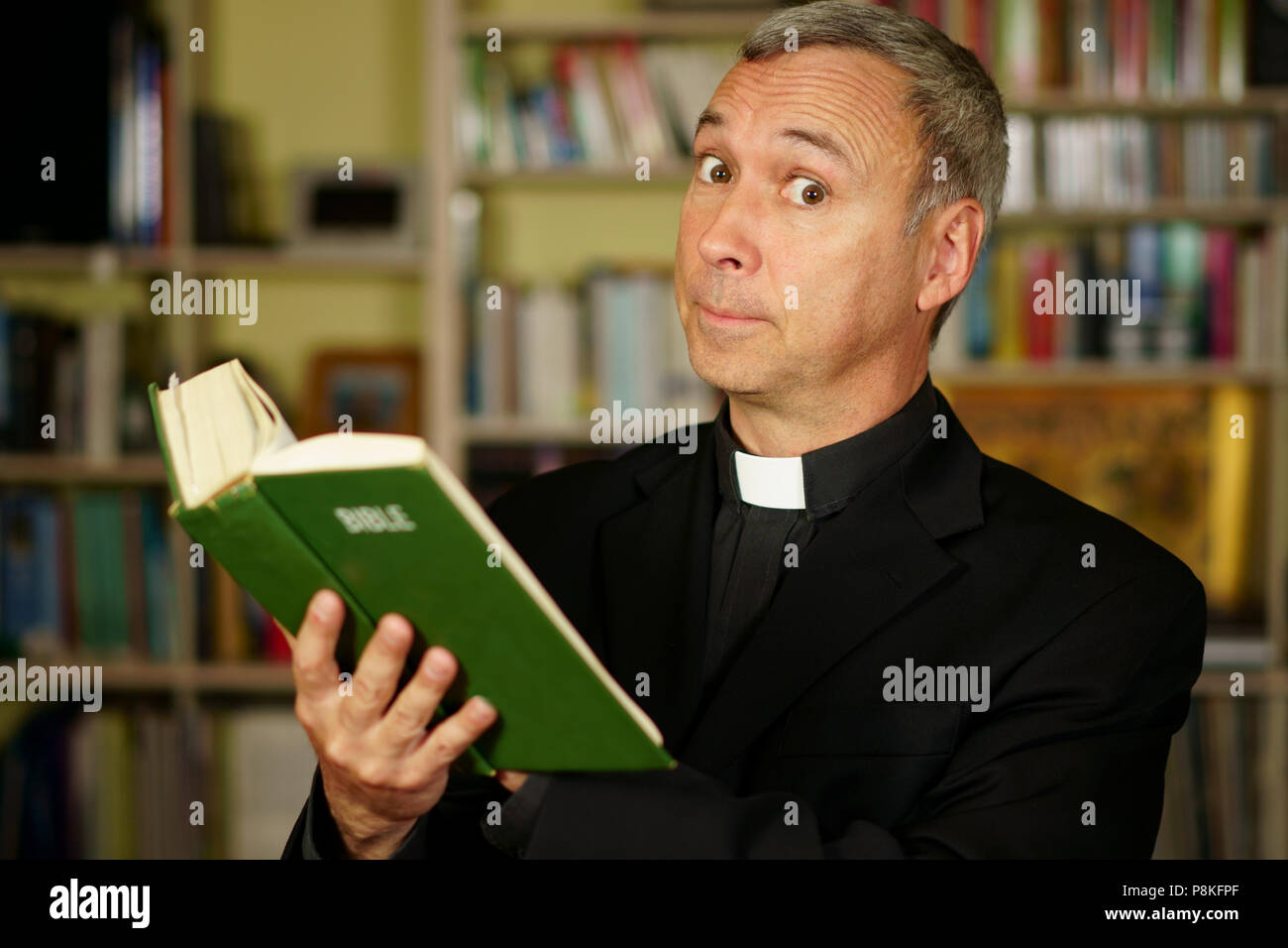 A good looking serious catholic priest is studying, reading the Bible ...