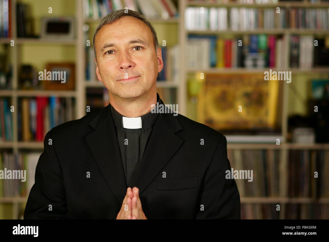 A good looking catholic priest is praying into his library. He looks at ...