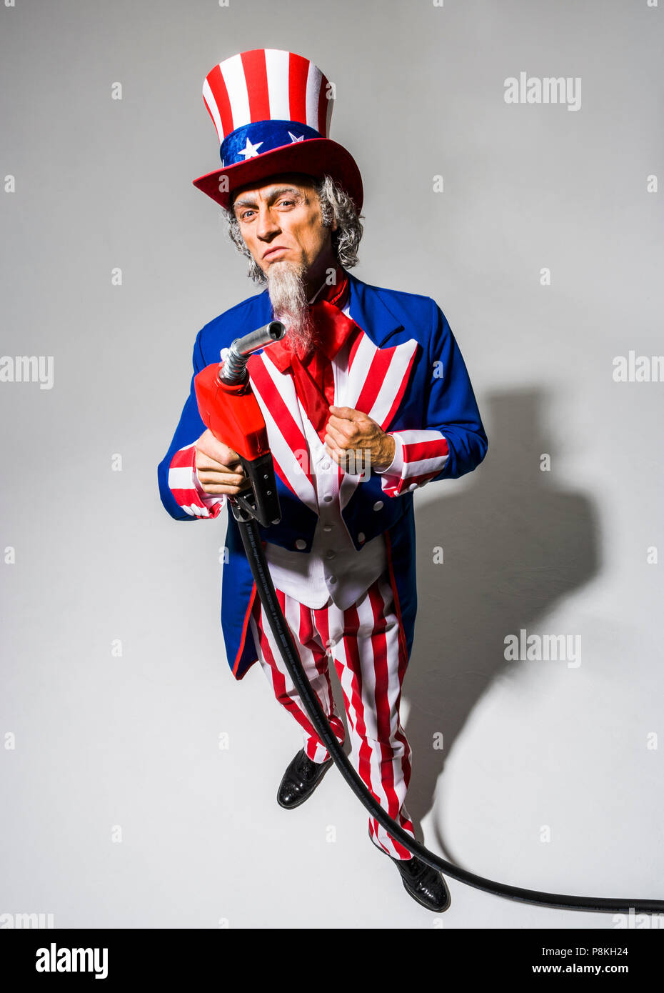 Uncle Sam standing with a gas pump nozzel held in front of him. Conceptual shot depicting the ...