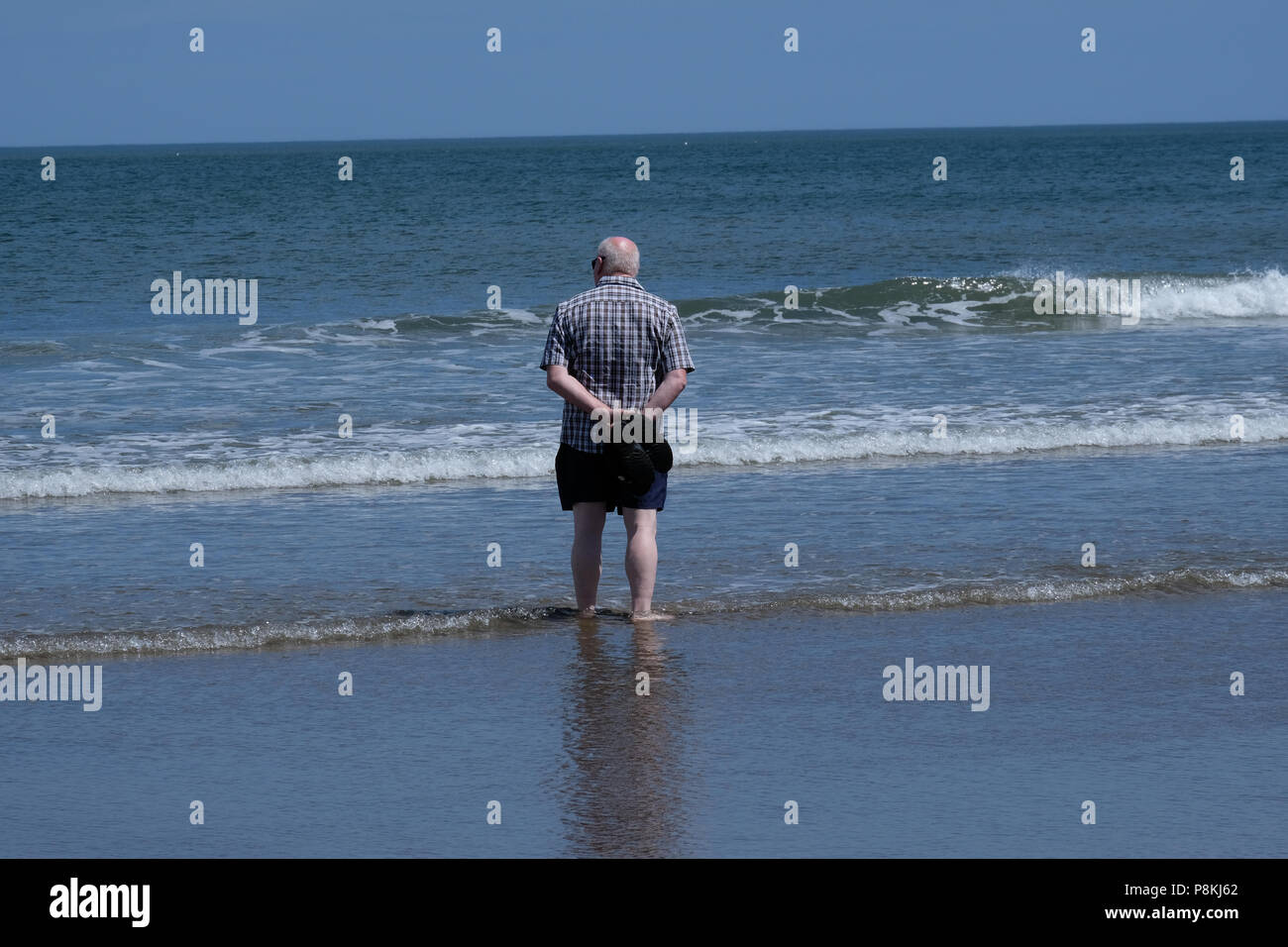 Single elderly man holding shoes behing his back and standing with his ...