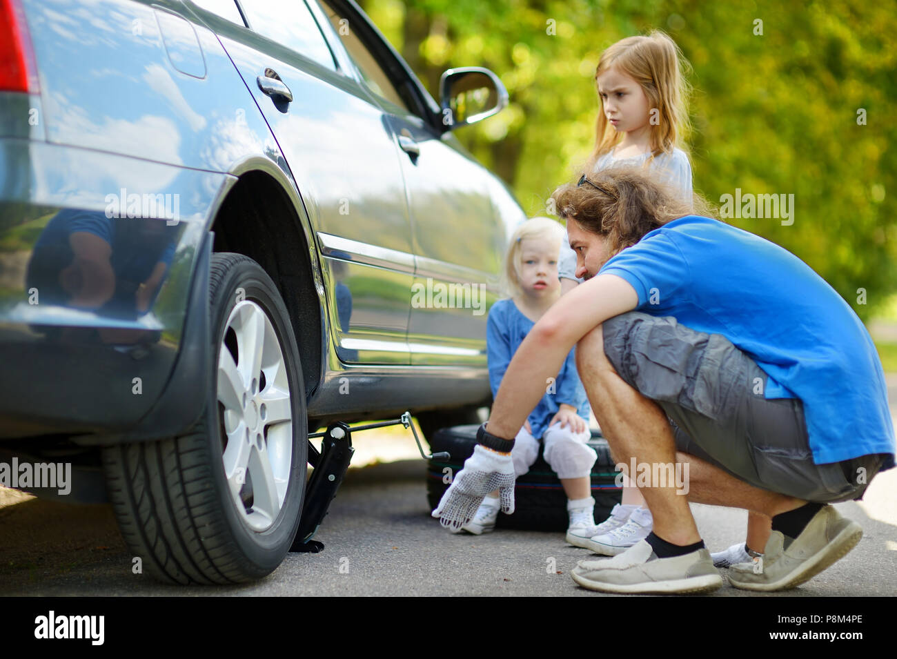 Young father and his two daughters changing a car wheel outdoors on ...