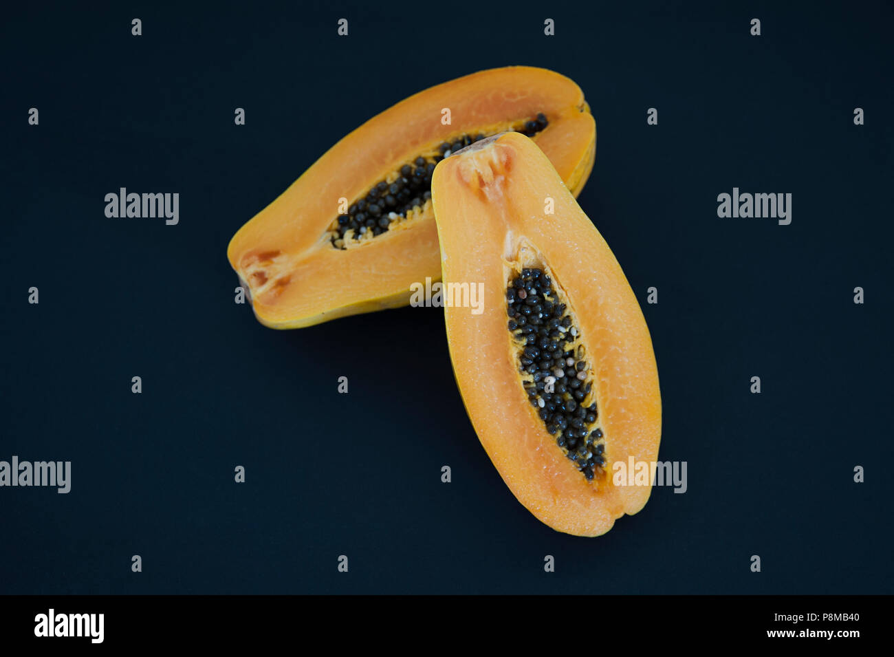 Papaya cut in two halves, with seeds and based on a dark blue ...