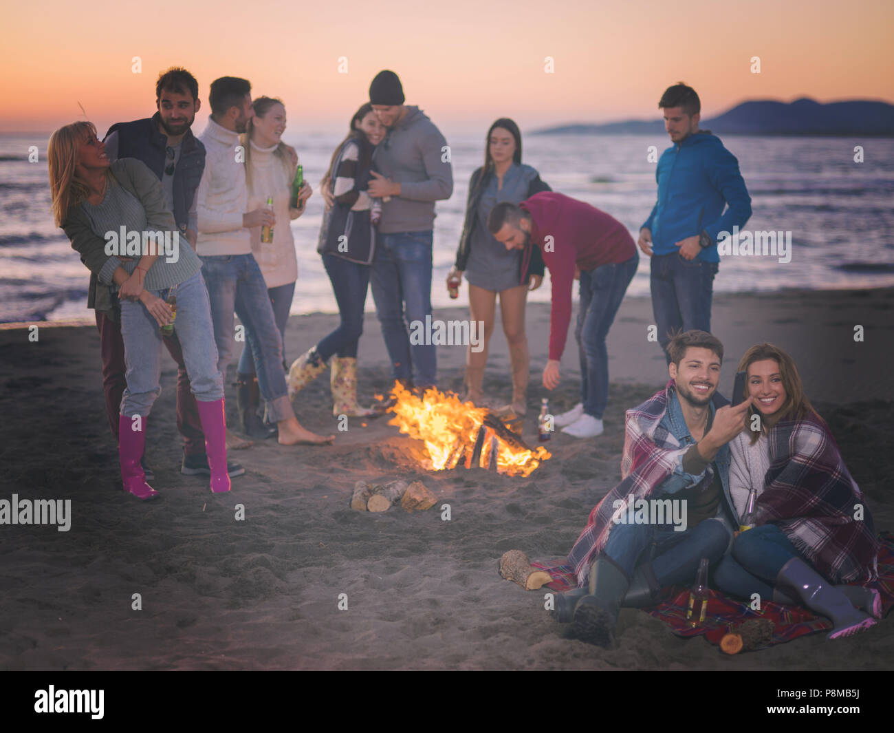 Couple using cell phone during beach party with friends drinking beer ...