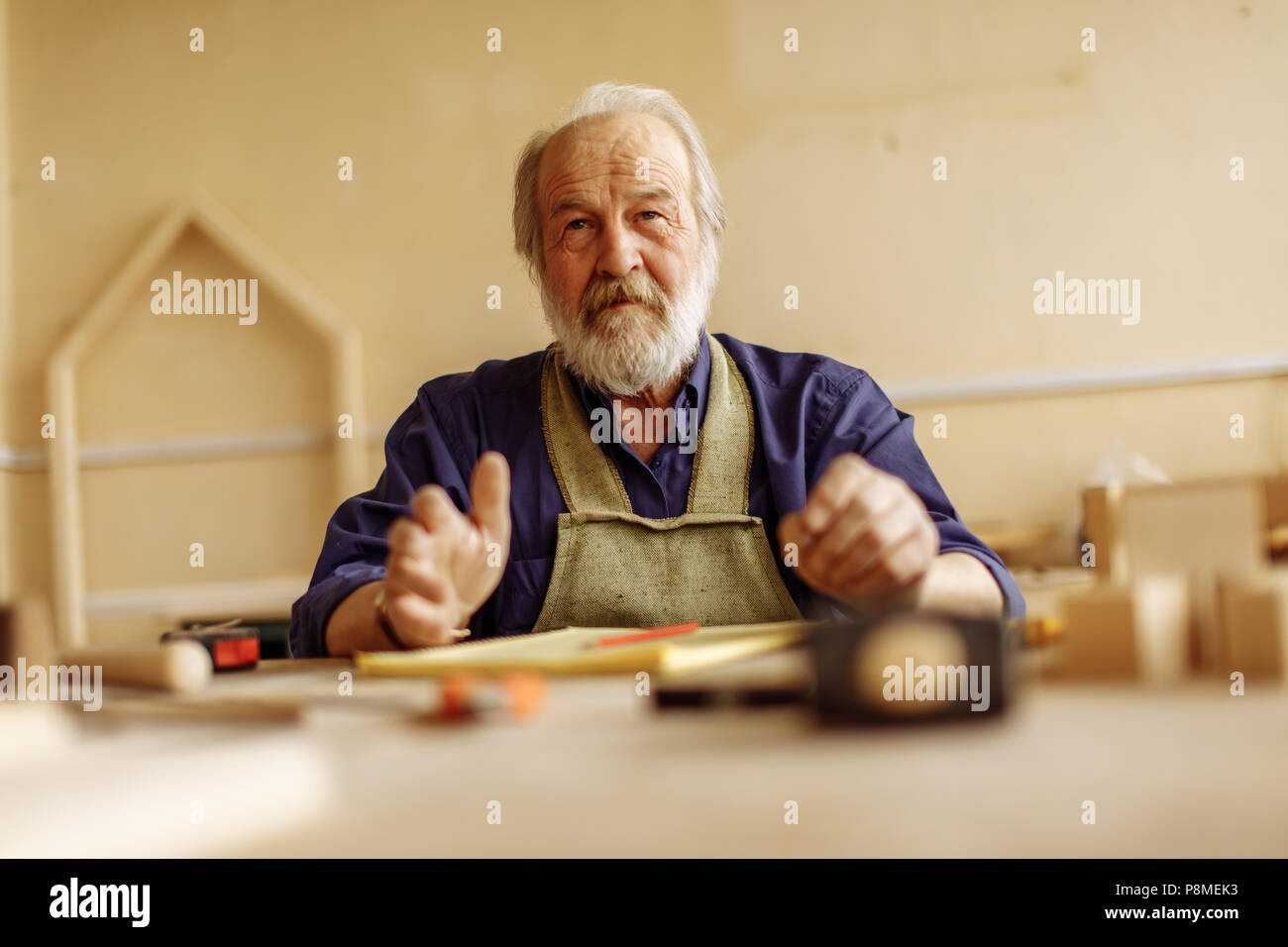 old man with working uniform is sitting in the home workshop.old seller ...