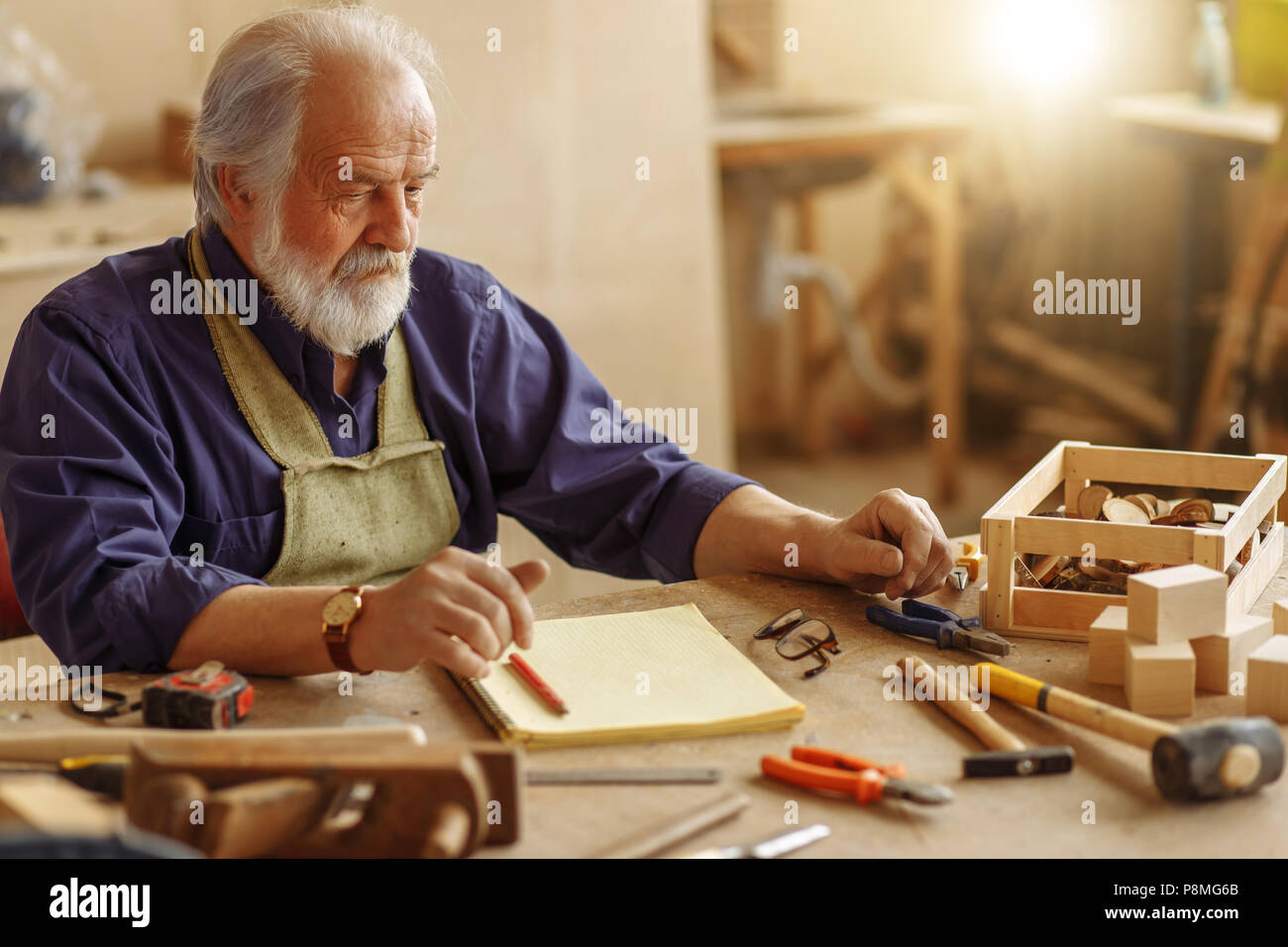 old experienced carpenter sitting at the messy table at workplace.close ...