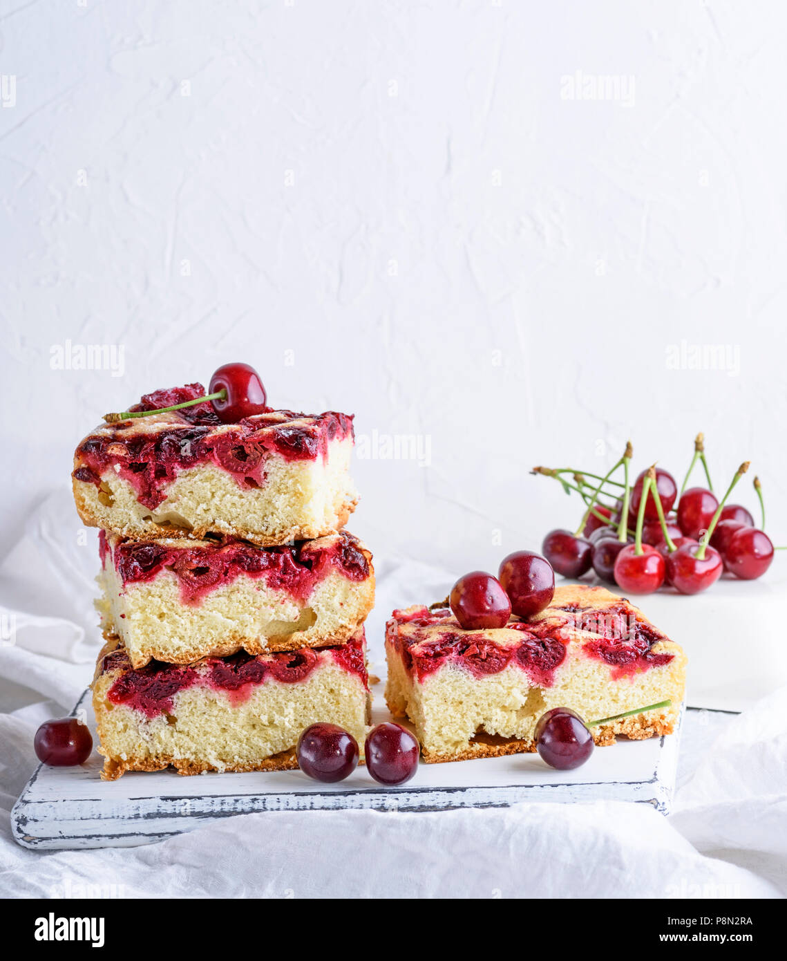 baked square pieces of a biscuit pie with cherries on a white wooden ...