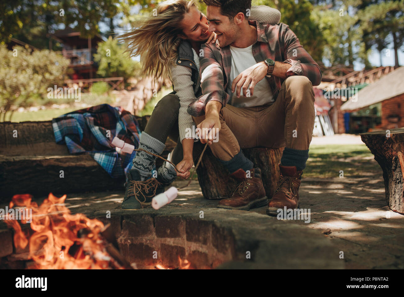 Romantic couple sitting by bonfire and roasting marshmallows on fire ...
