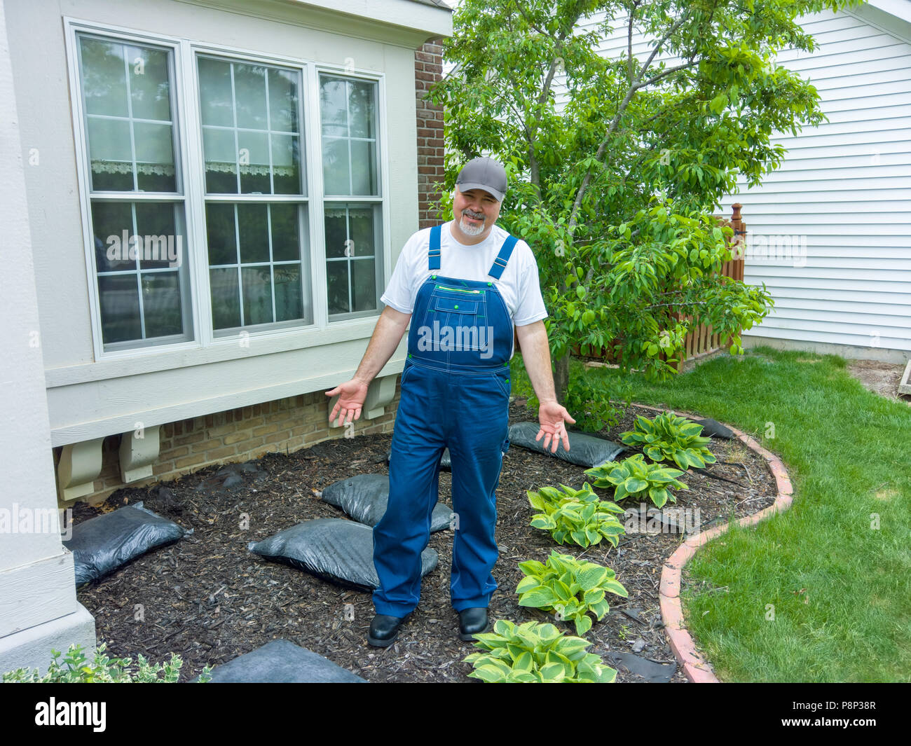 Man standing in a flowerbed with bags of mulch gesturing with his hands ...