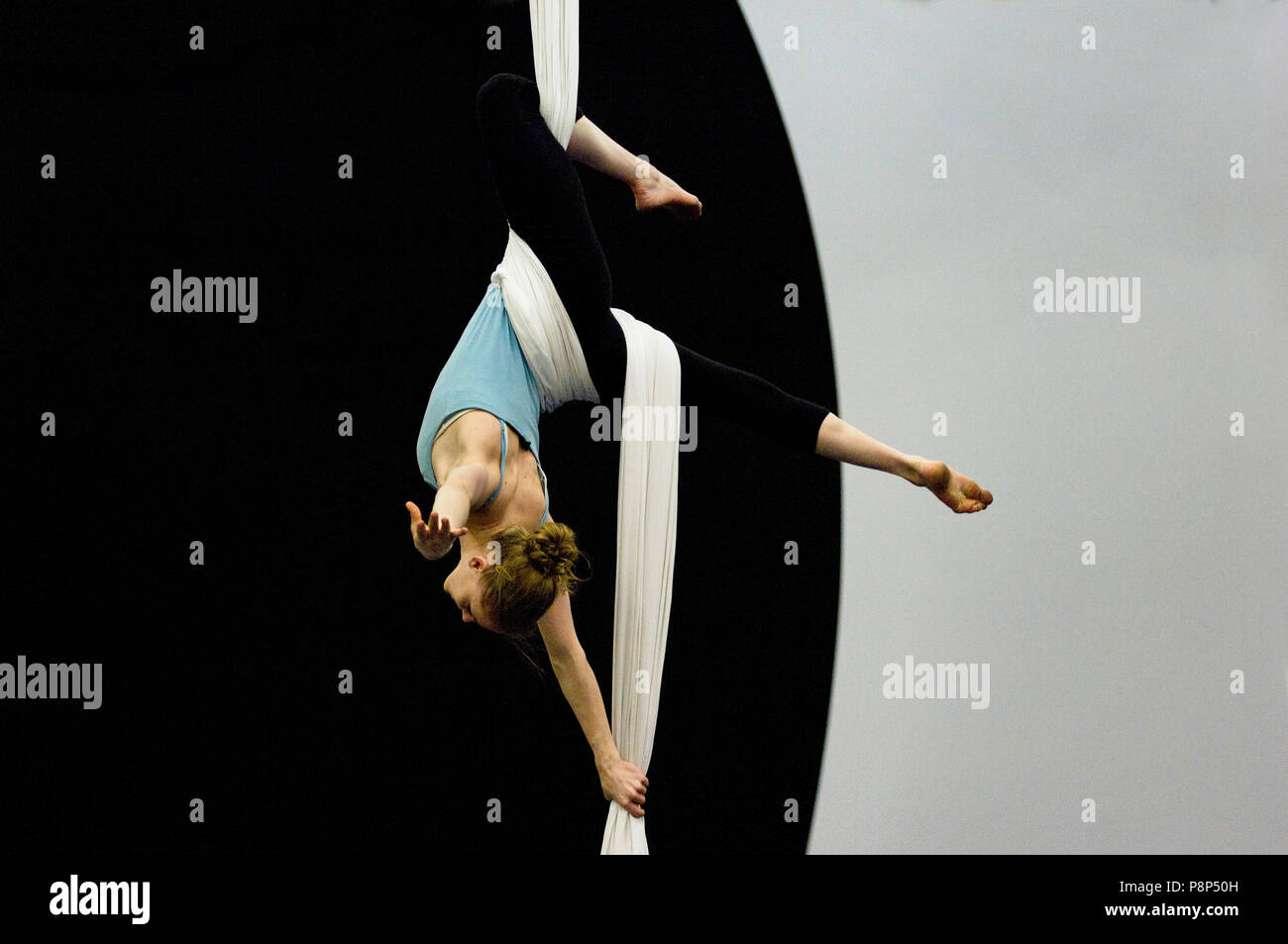 A female acrobat suspends herself upside down by wrapping aerial silks ...