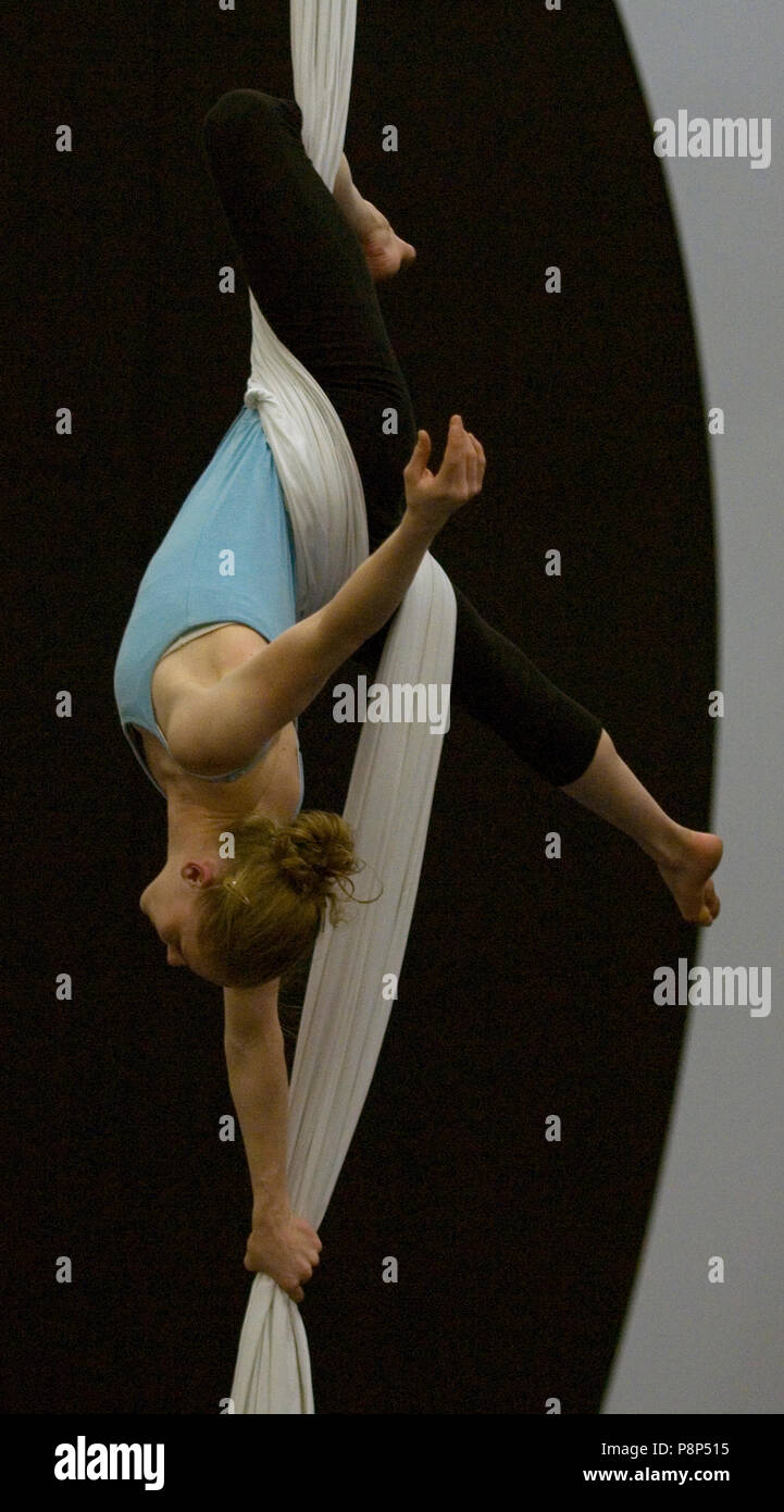 A female acrobat suspends herself upside down by wrapping aerial silks ...