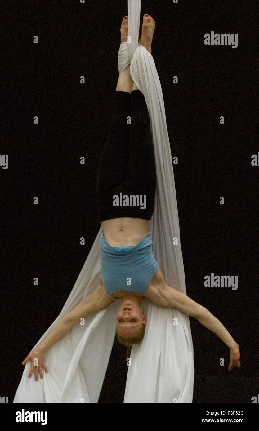 A female acrobat suspends herself upside down by wrapping aerial silks ...