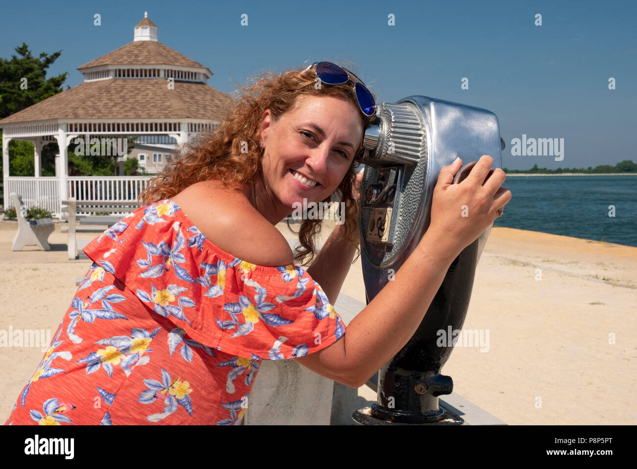woman uses coin operated binocular to observe landscape, ocean, boats ...
