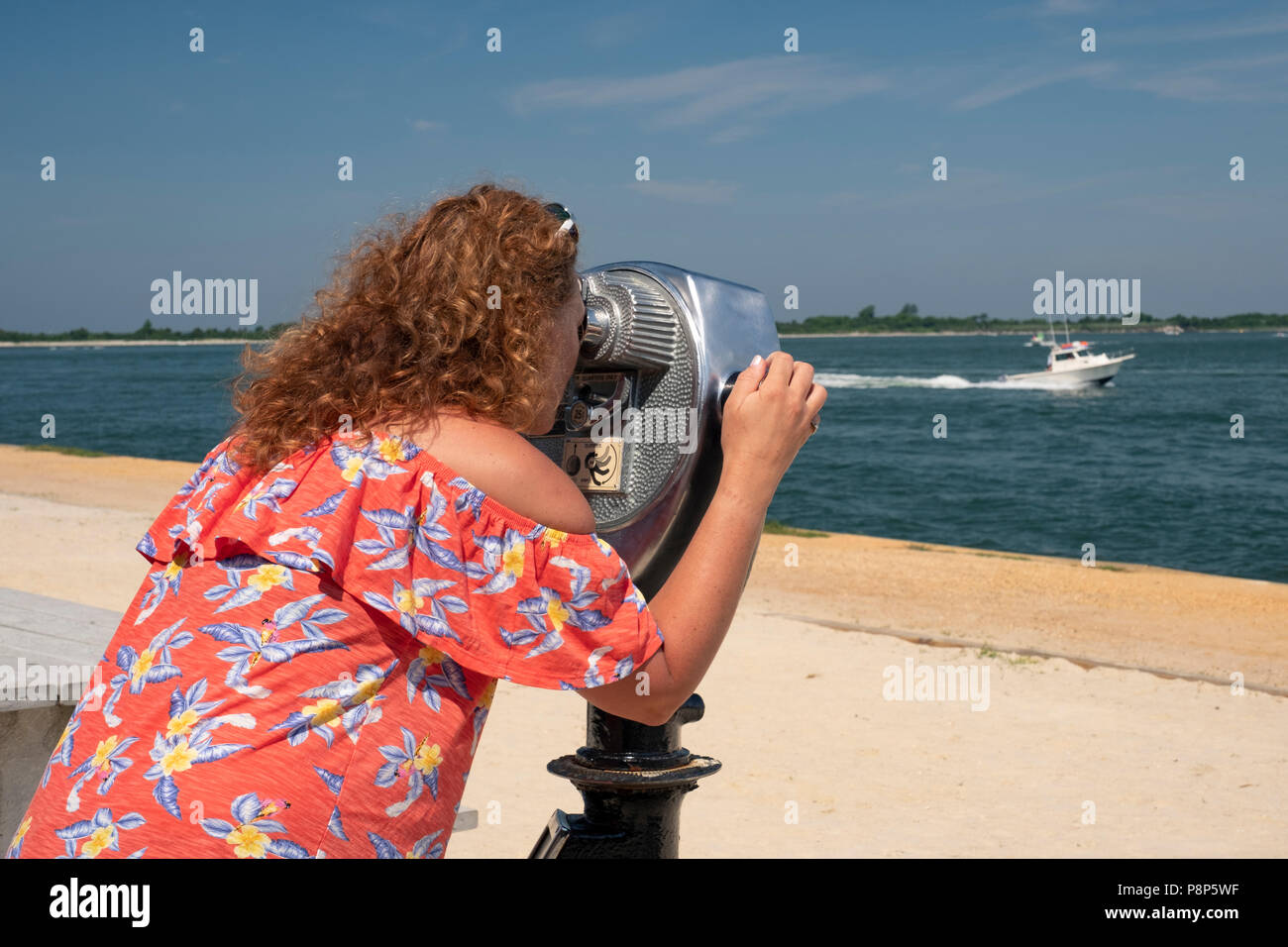 woman uses coin operated binocular to observe landscape, ocean, boats ...