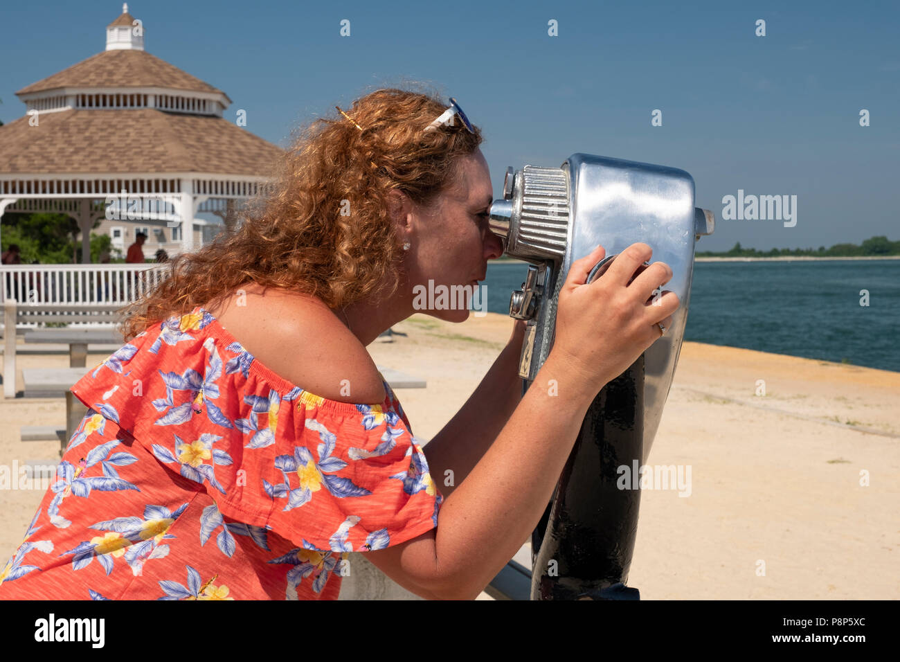 woman uses coin operated binocular to observe landscape, ocean, boats ...