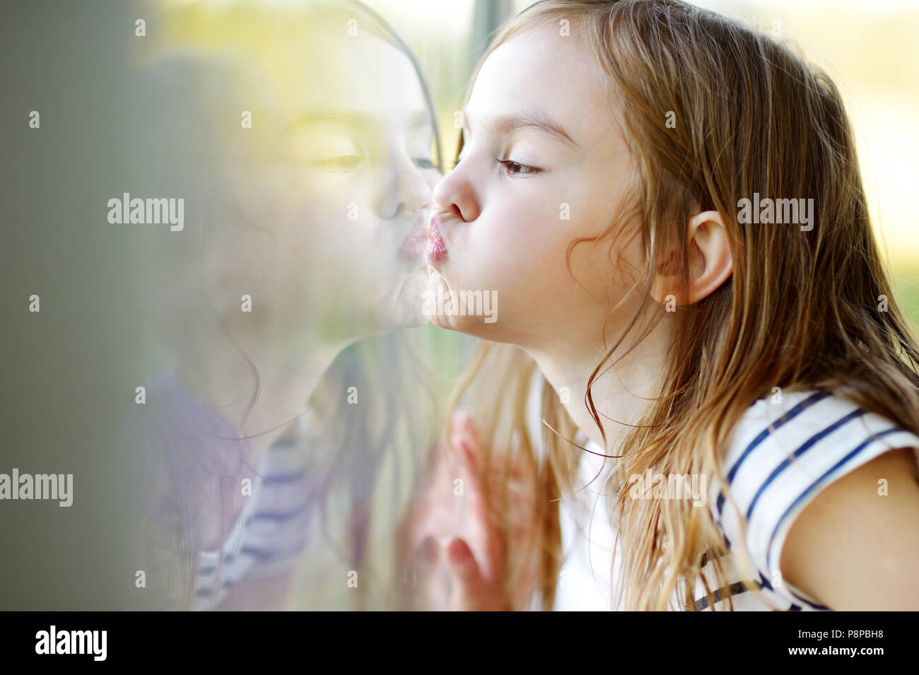 Cute funny little girl kissing her reflection on a window glass Stock ...