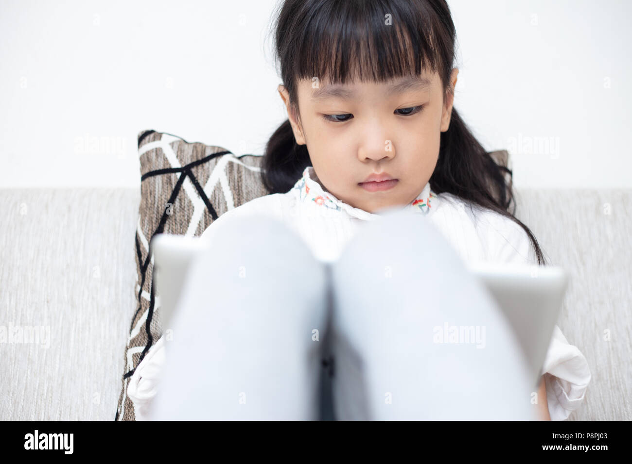 Asian Chinese little girl sitting on the sofa and playing tablet in the ...