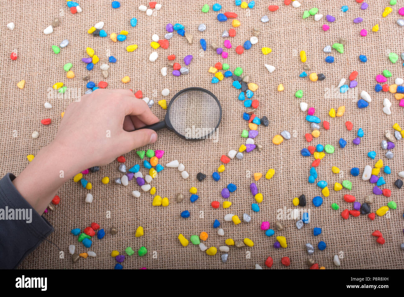 Hand holding a magnifying glass amid Colorful pebbles Stock Photo - Alamy
