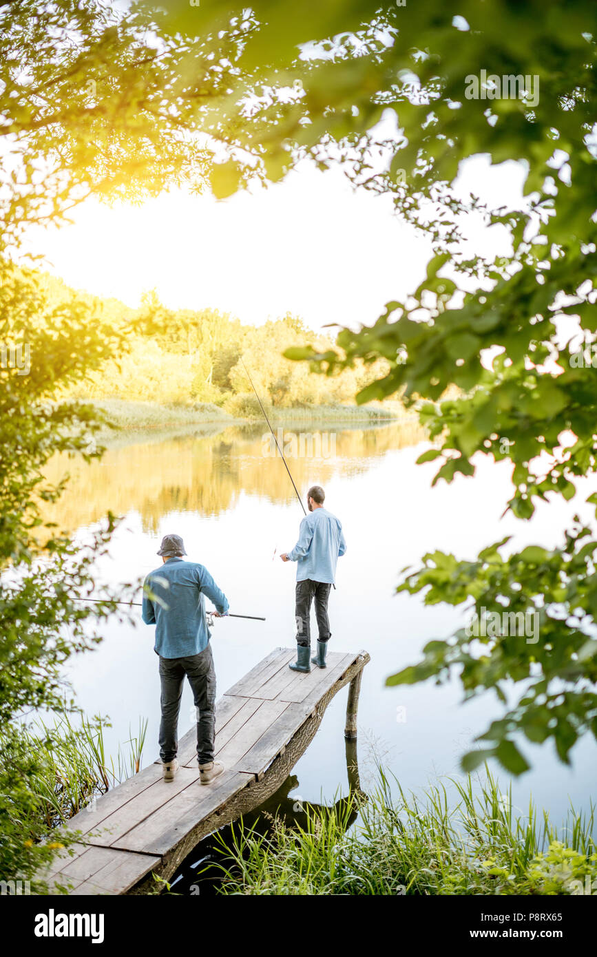 Two male friends fishing together standing on the wooden pier during ...