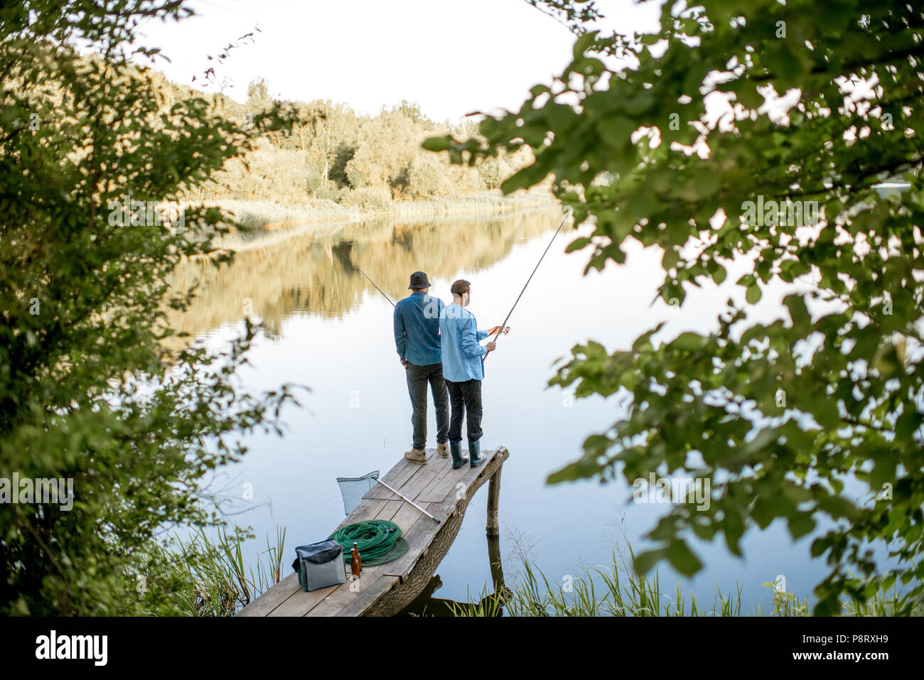 Two male friends fishing together standing on the wooden pier during ...
