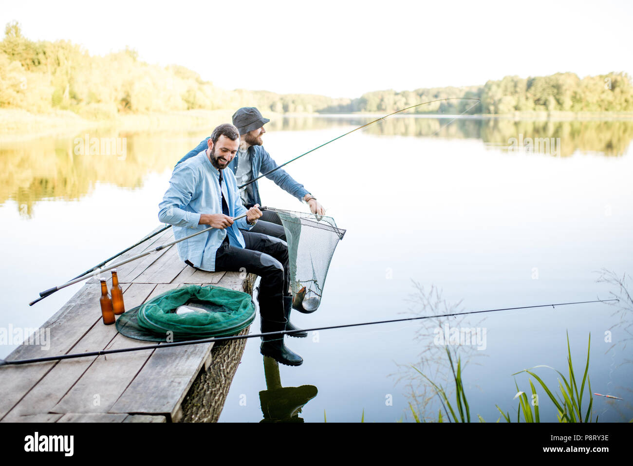 Two friends catching fish with fishing net and rod sitting on the ...