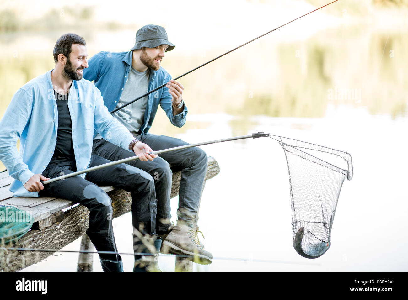 Two friends catching fish with fishing net and rod sitting on the ...