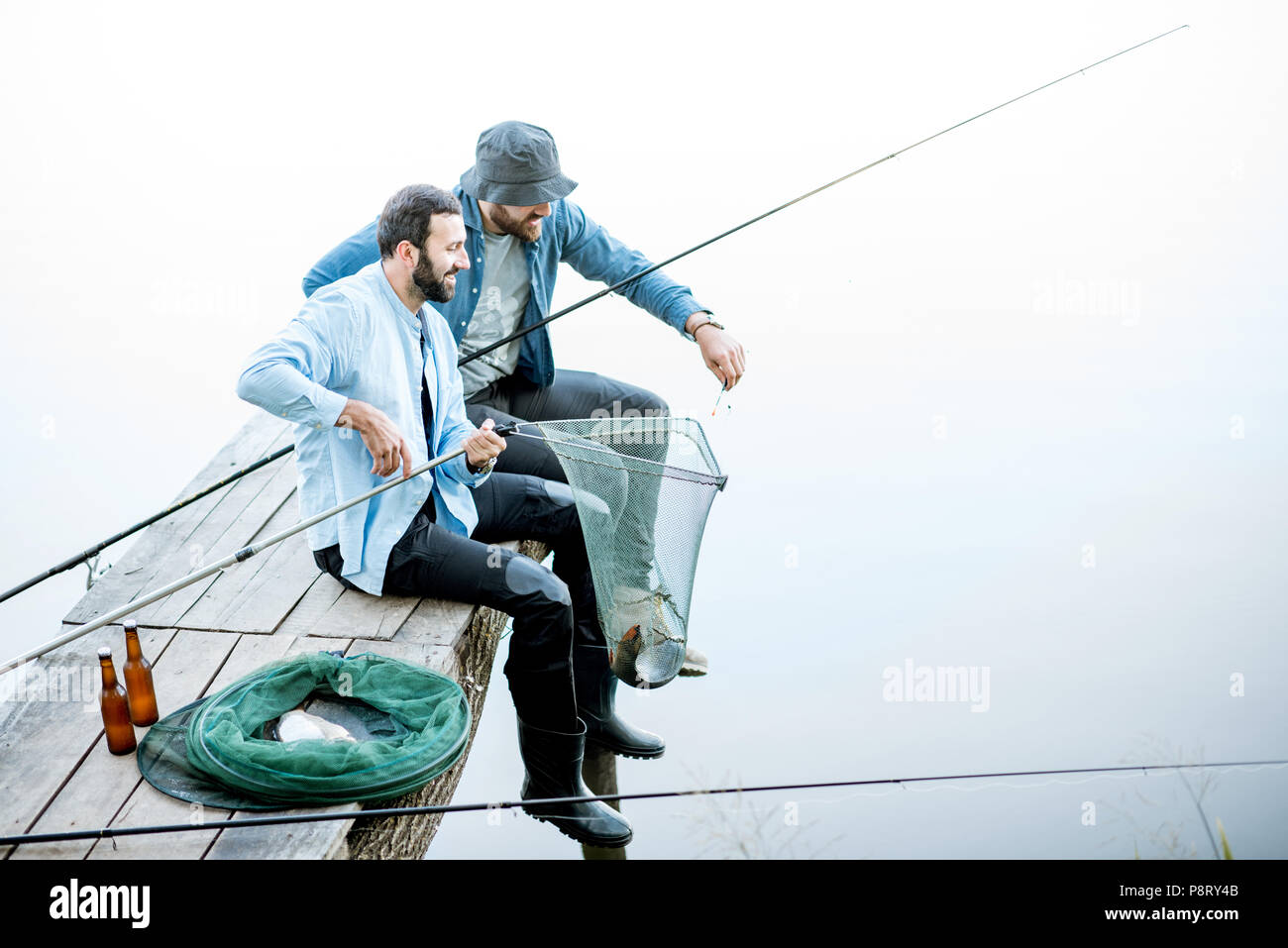 Two friends catching fish with fishing net and rod sitting on the ...