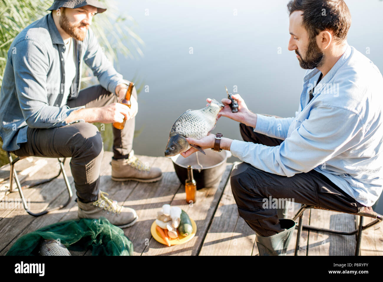 Two friends sitting together with beer and fish on the picnic while ...