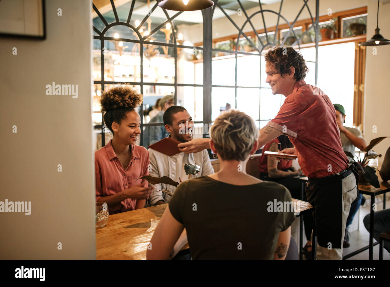 Group of smiling friends ordering food from a bistro waiter Stock Photo ...
