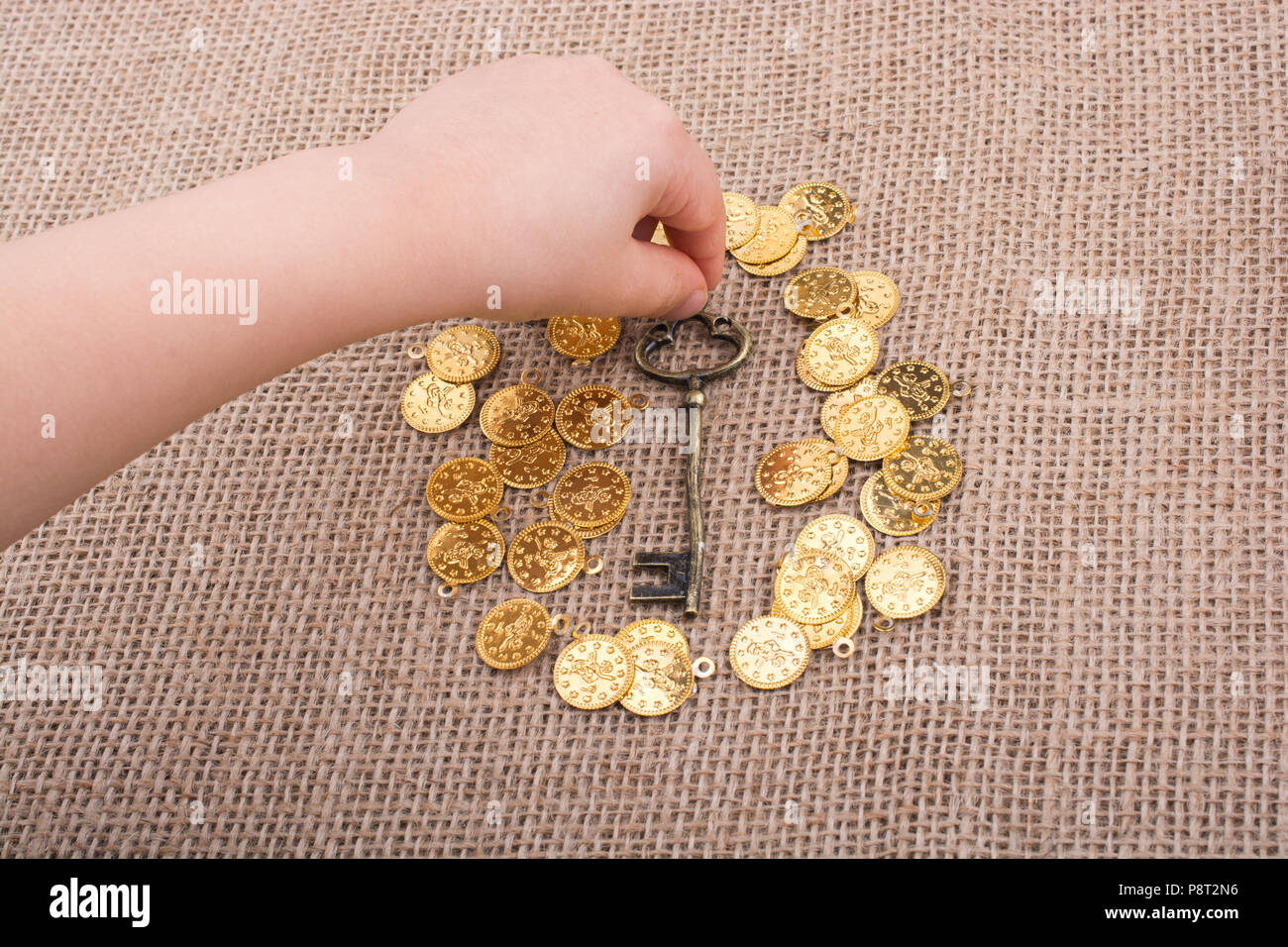 Hand holding a retro styled key over fake gold coins Stock Photo - Alamy