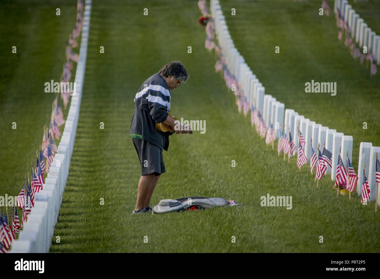 Man playing on an ukulele in the midst of rows of tombstones decorated ...
