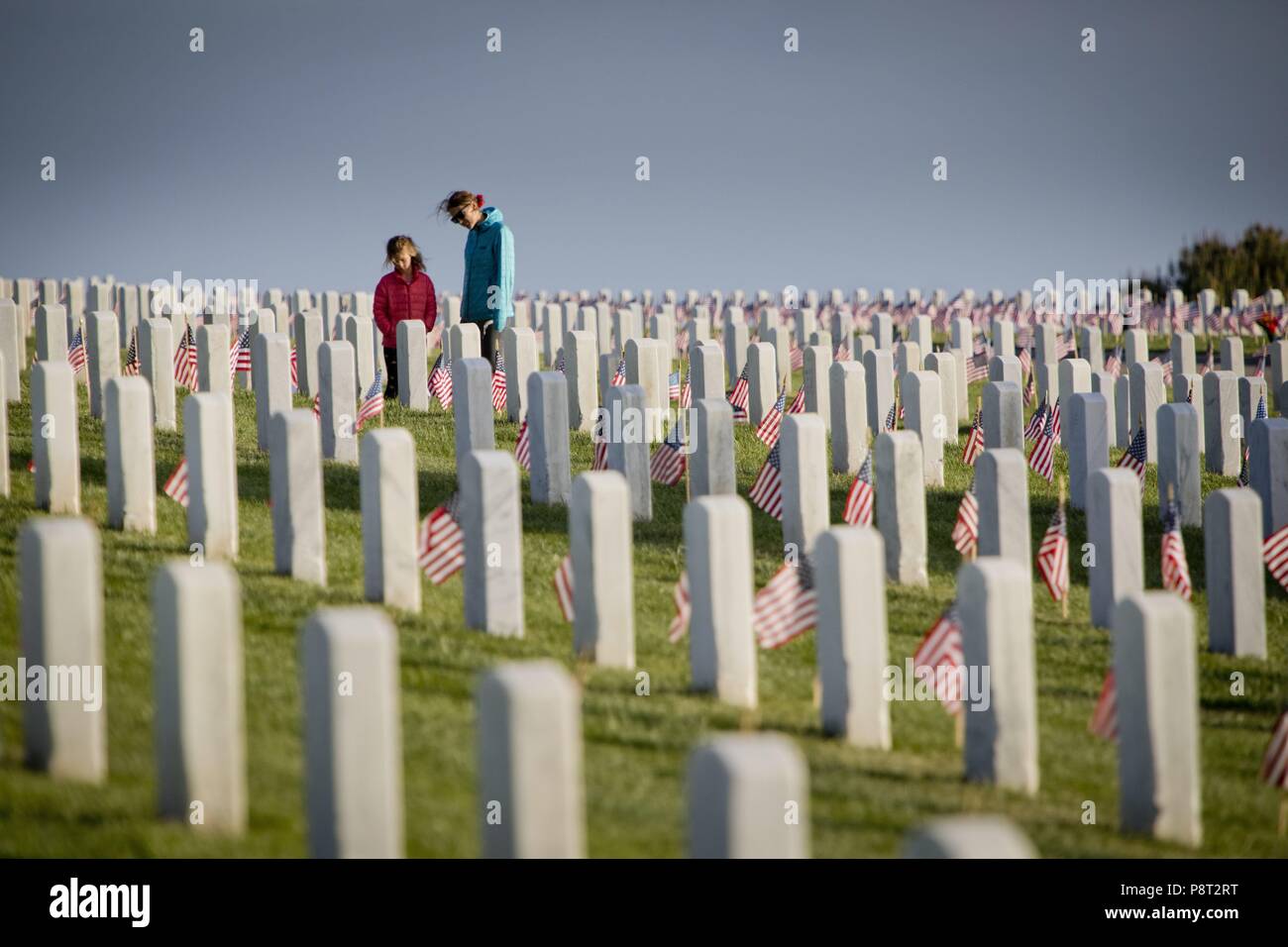 Mother and daughter in the midst of rows of tombstones decorated with ...
