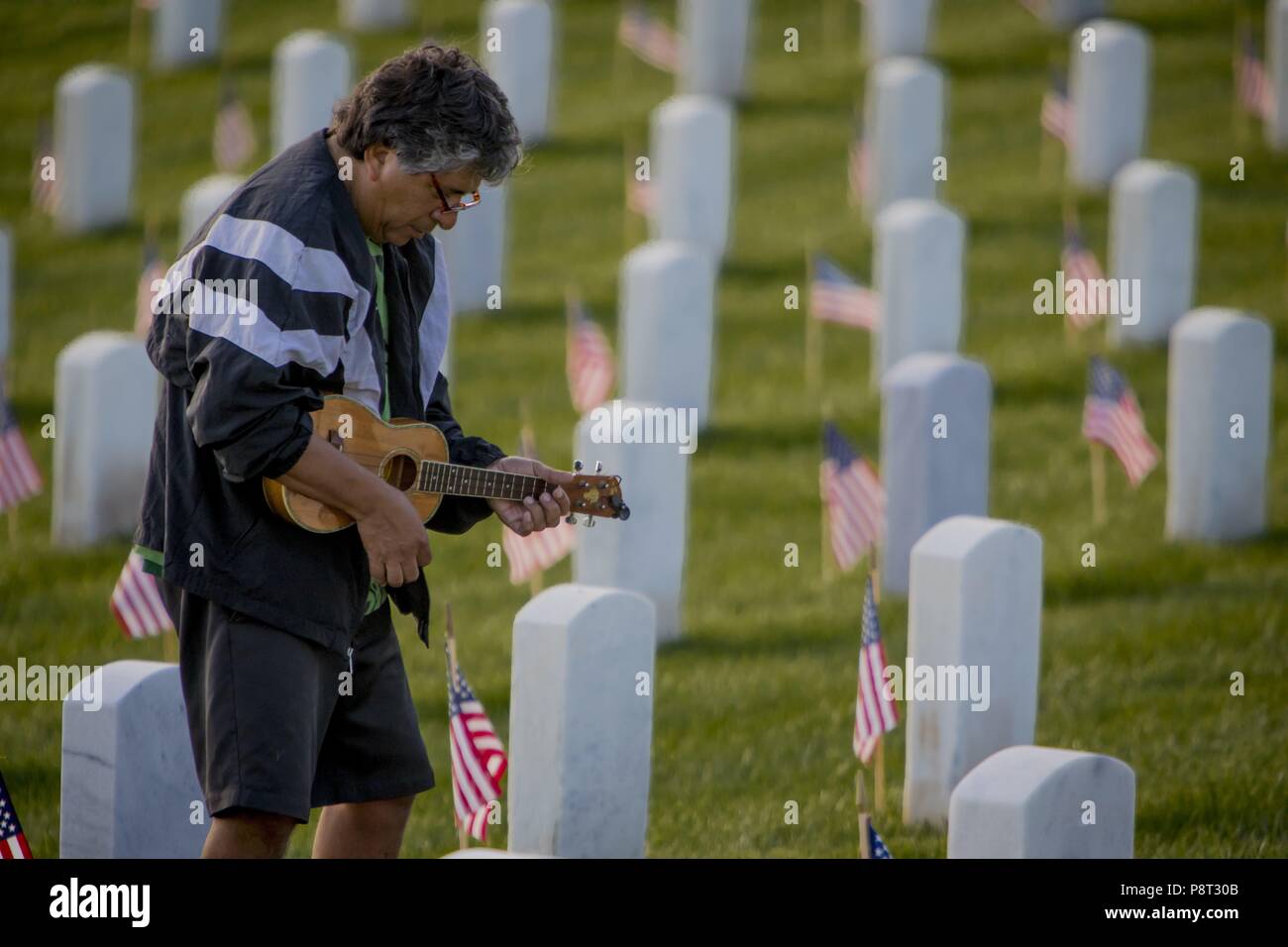 Man playing on an ukulele in the midst of rows of tombstones decorated ...
