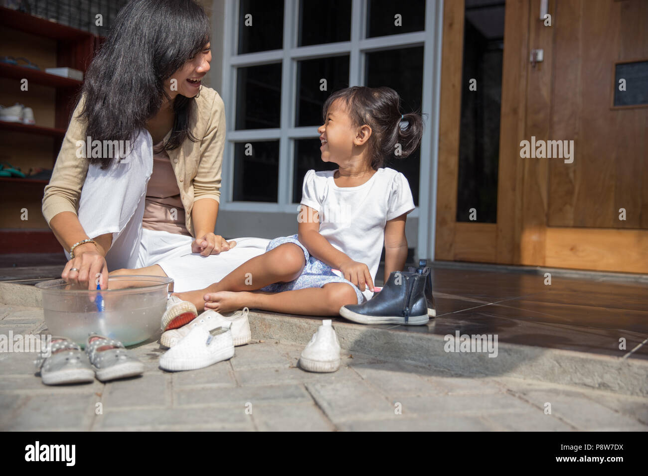 happy asian mother with her toddler girl washing their shoes together ...