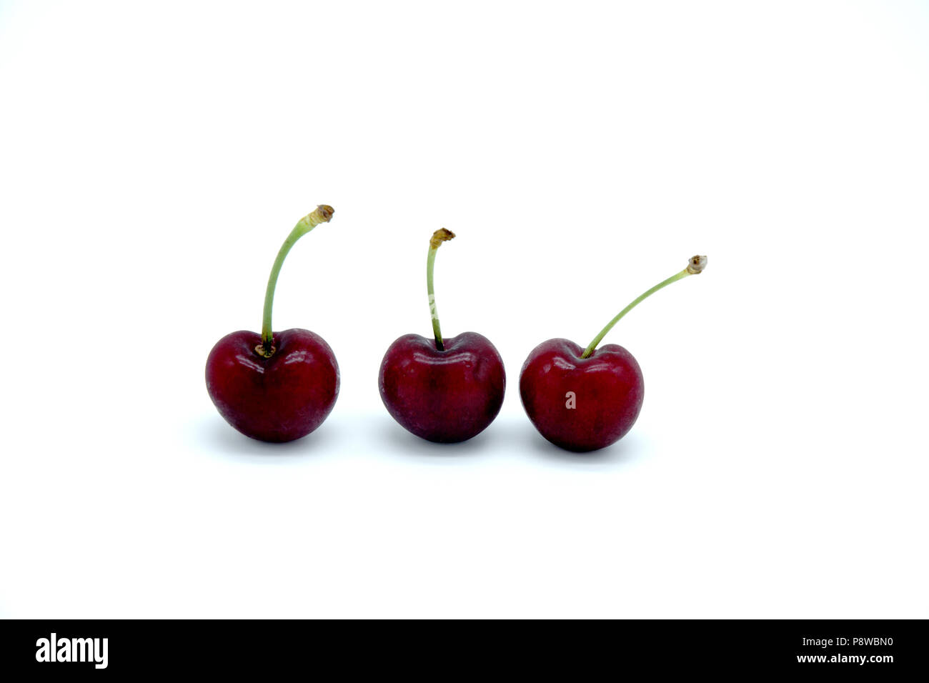 3 cherries on a row on a white background Stock Photo - Alamy