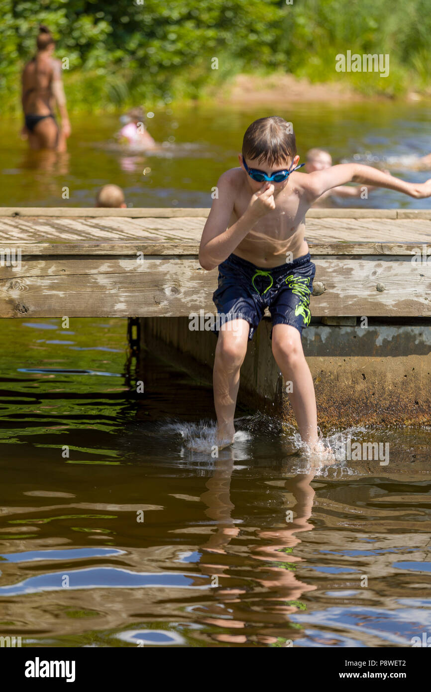 Young boy jumping into lake water from Jetty Stock Photo - Alamy