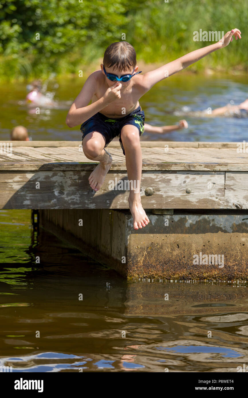 Young boy jumping into lake water from Jetty Stock Photo - Alamy