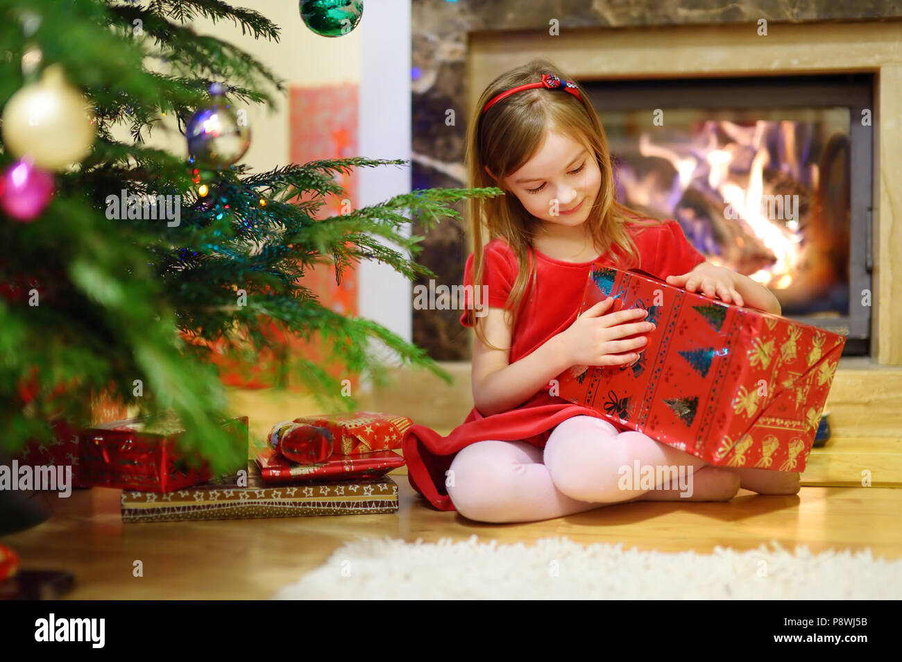 Adorable little girl opening Christmas gifts by a Christmas tree in ...